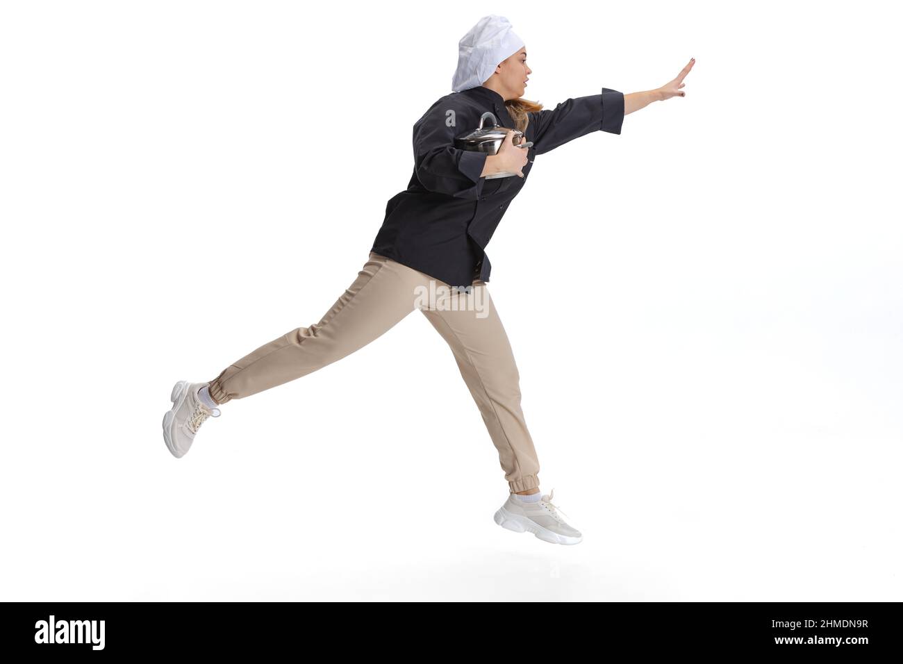 Studio shot of young woman, lady-cook, chef in black uniform running ...