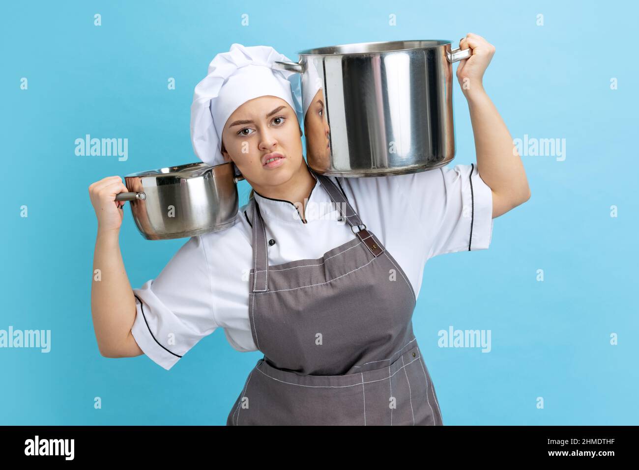 Portrait of young annoyed woman, lady-cook, chef in white uniform with ...
