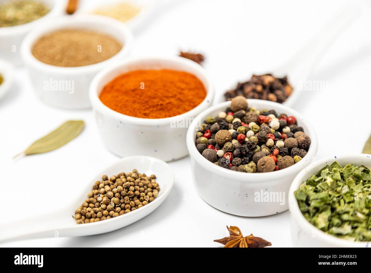 Various spices for cooking, laid out in white bowls and spoons, close ...