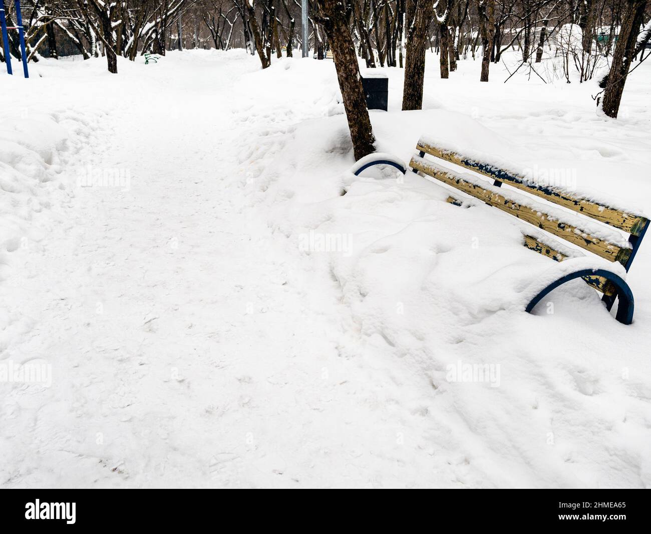 path trodden in snow near snow-covered bench in city park on overcast ...
