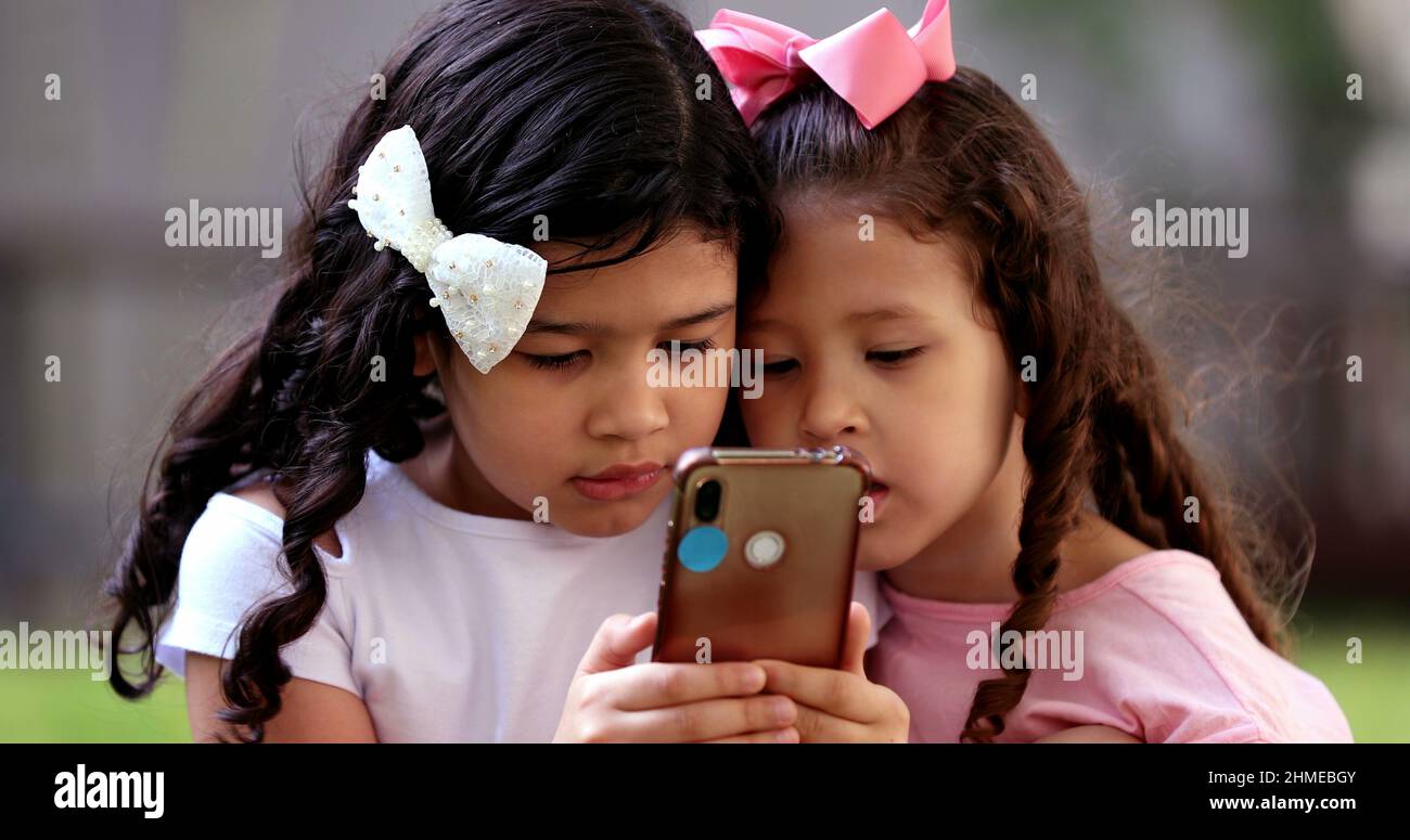 Children addicted to cellphone, two little girls looking at smartphone ...