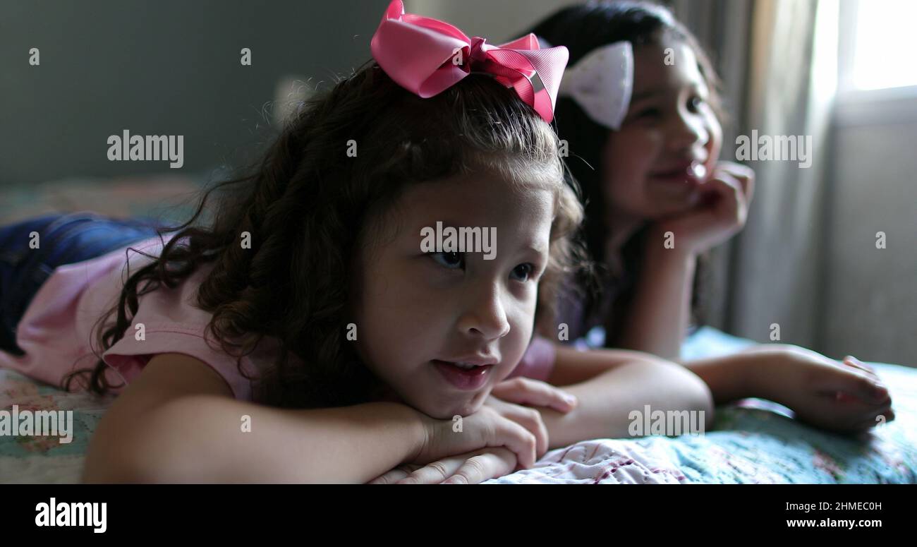 Children watching movie at home, girls lie in bed hypnotized by screen ...