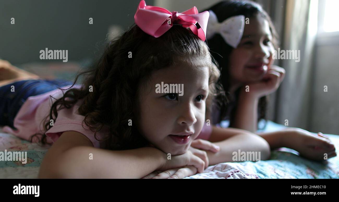 Children watching movie at home, girls lie in bed hypnotized by screen ...