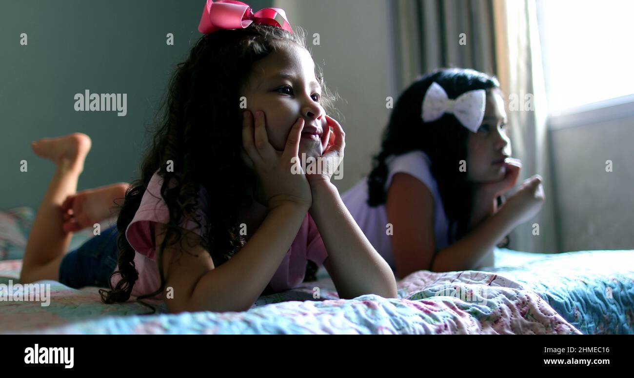 Children watching movie at home, girls lie in bed hypnotized by screen ...