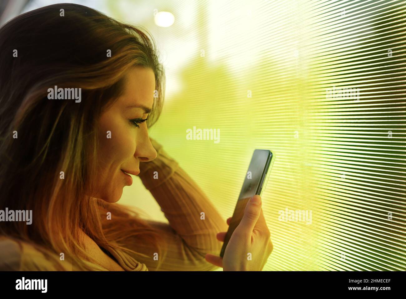 woman looking at her cell phone screen on a modern wall with yellow LED ...
