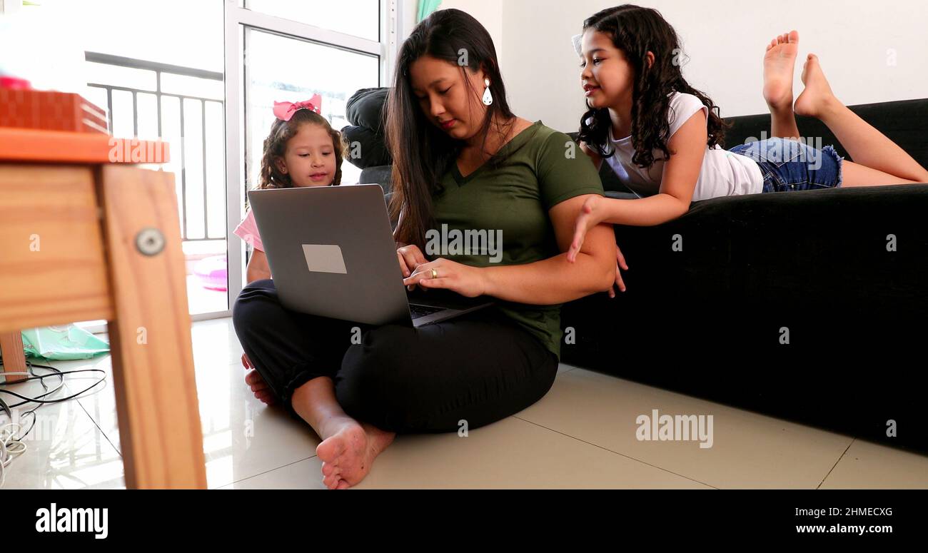 Mother multi-tasking, using computer laptop at home while parenting two ...