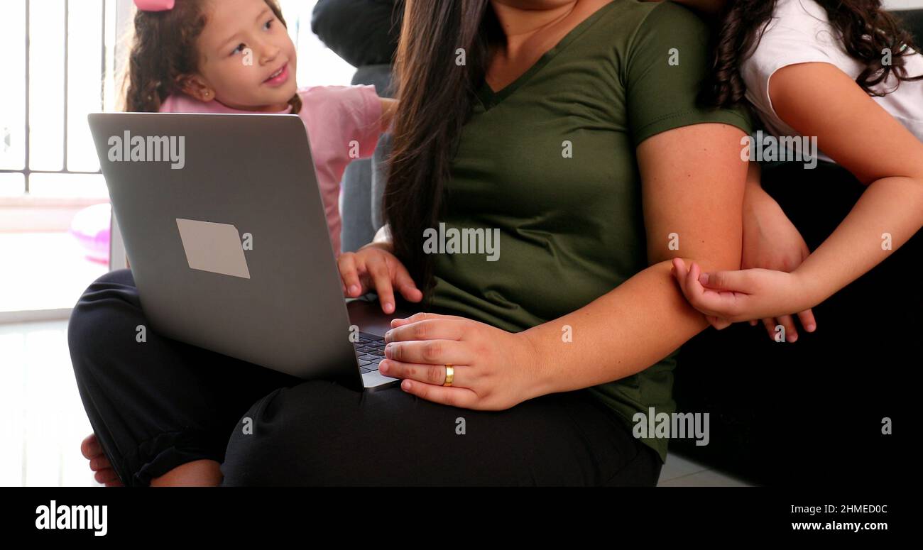 Mother multi-tasking, using computer laptop at home while parenting two ...