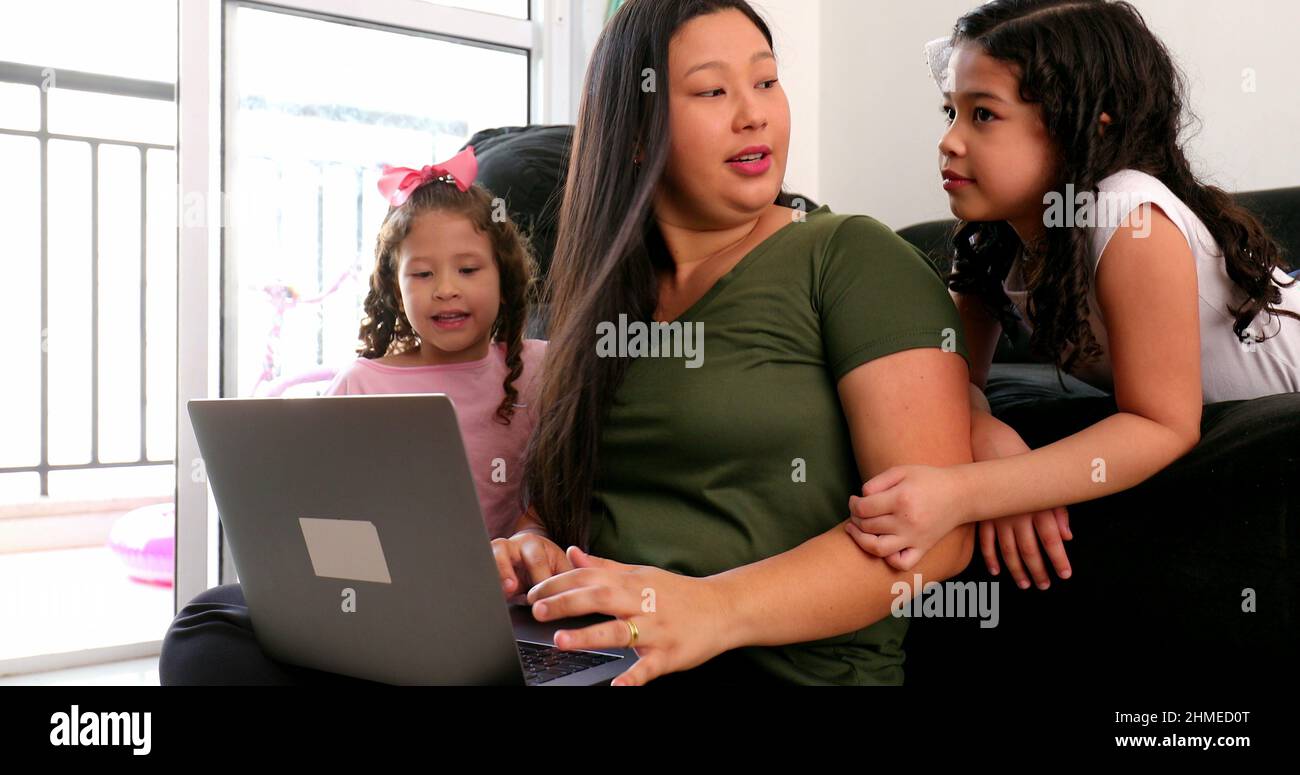 Mother multi-tasking, using computer laptop at home while parenting two ...