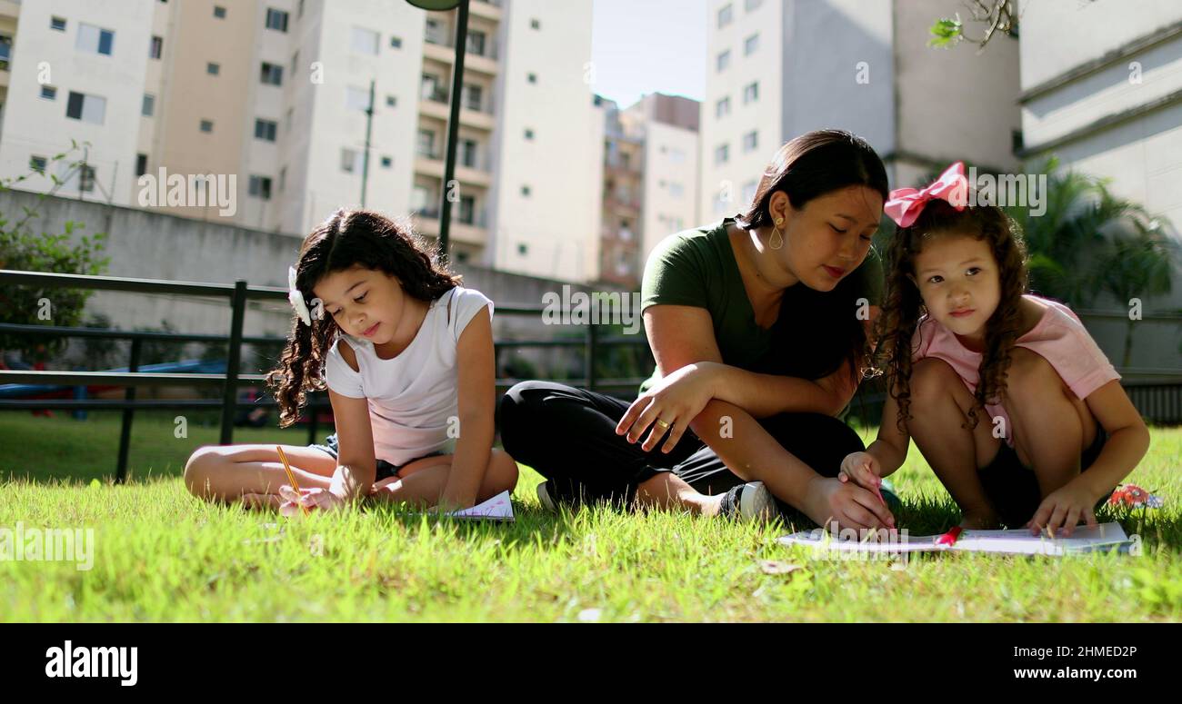 Parent helping children with study outside at park. Asian mother ...