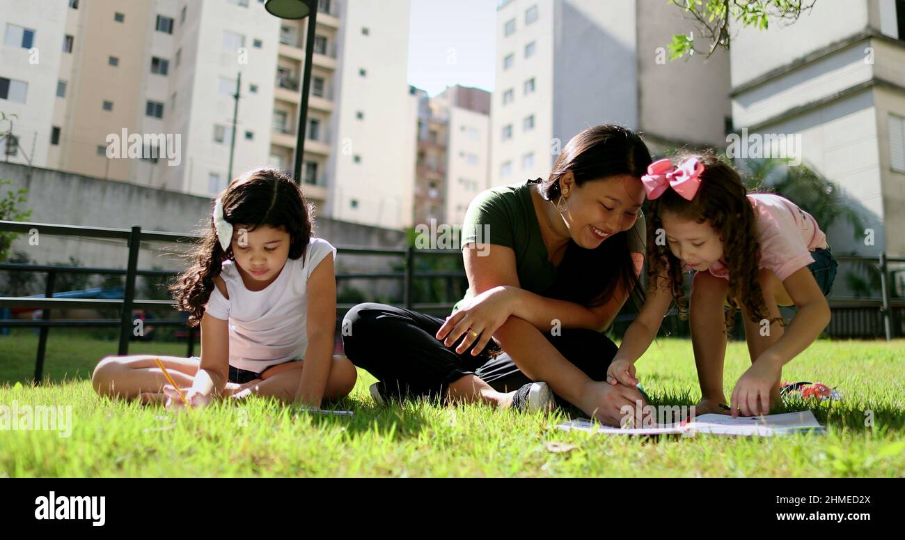 Parent helping children with study outside at park. Asian mother ...