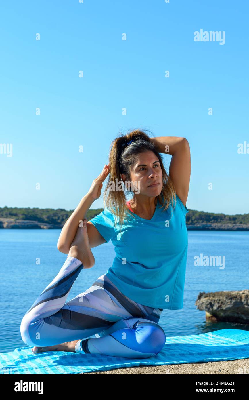 middle-aged fitness woman outdoors in front of the sea does yoga ...