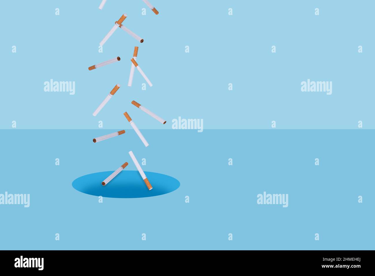 Cigarettes falling into a hole isolated on blue background. Giving up a ...