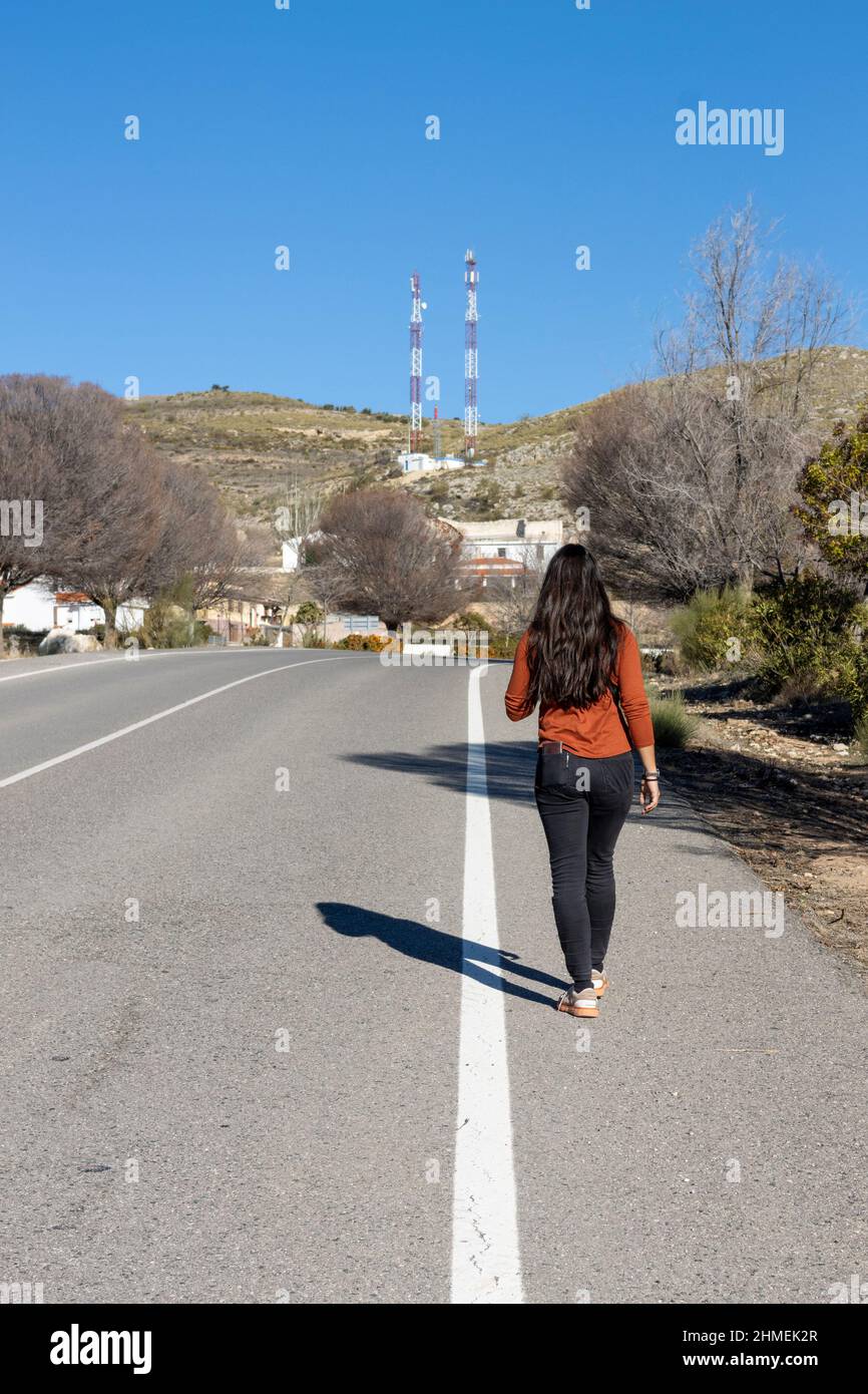 long-haired woman walking along the road shoulder. back view Stock ...