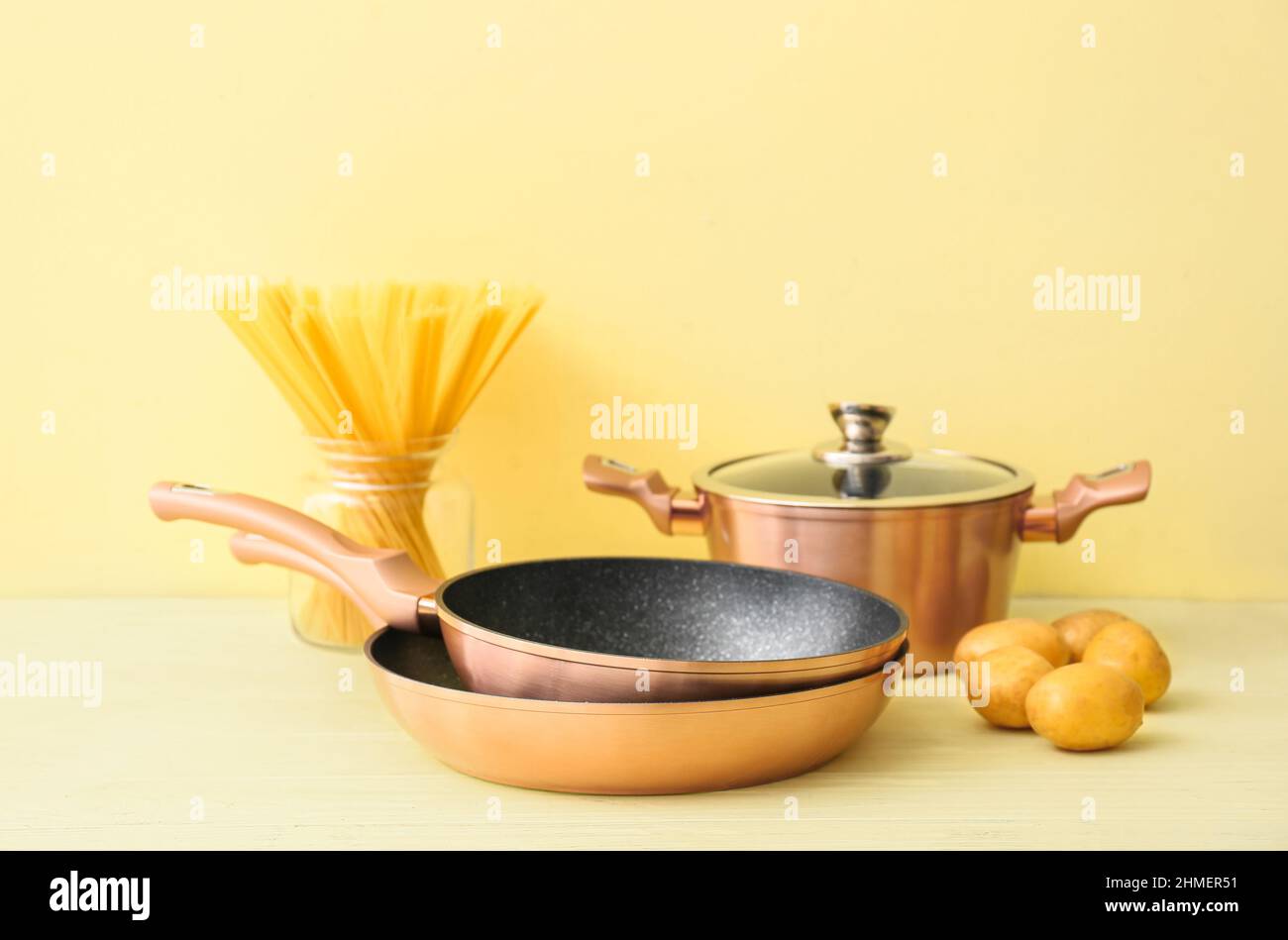 Copper frying pans, cooking pot, potatoes and jar with raw pasta on ...