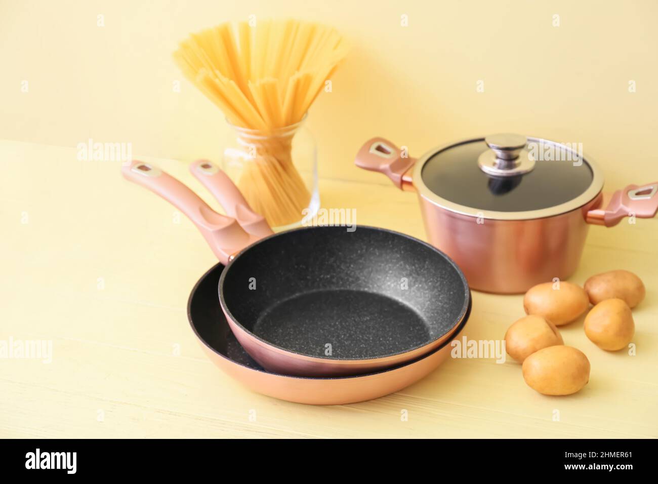 Copper frying pans, cooking pot, potatoes and jar with raw pasta on ...