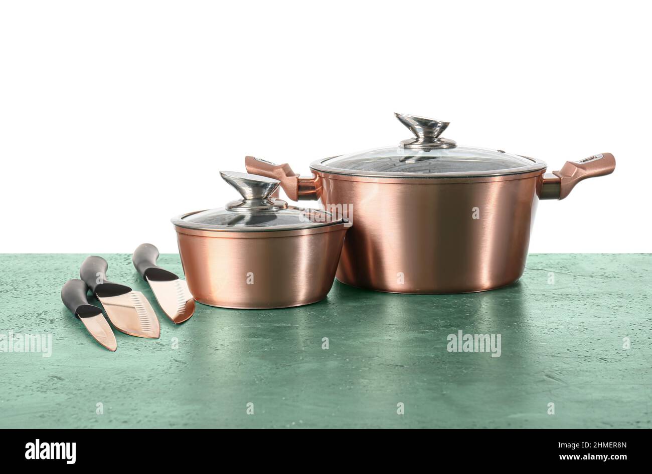 Copper cooking pots with knives on green table against white background ...