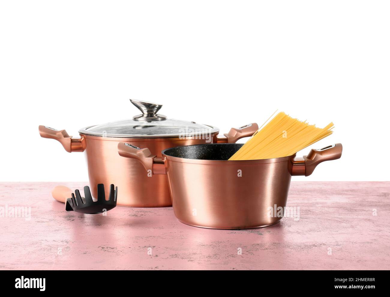 Copper cooking pots with raw pasta fork on pink table against white ...