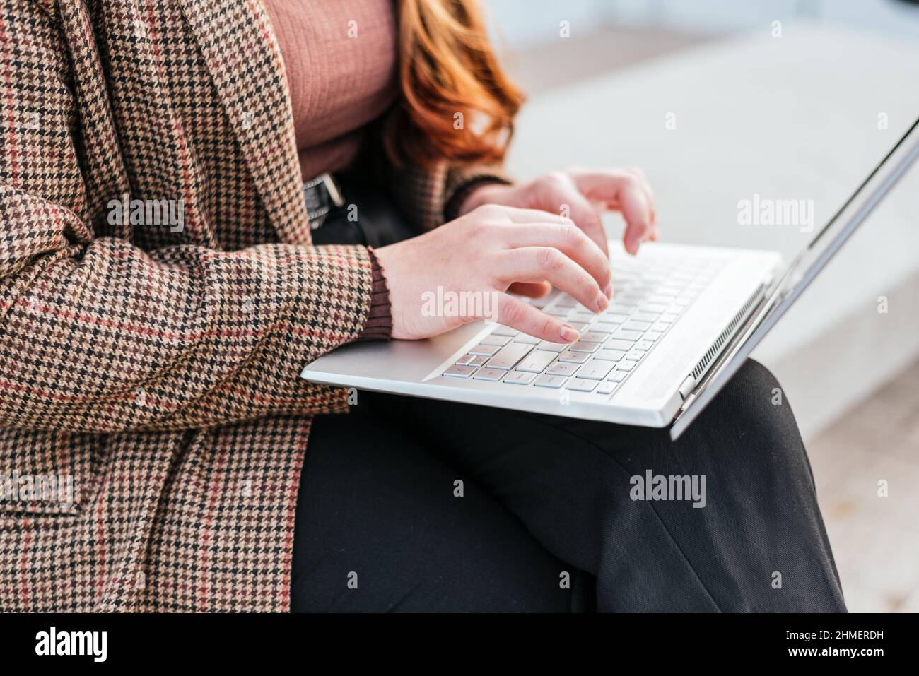 Unrecognizable woman in checkered coat typing on laptop keyboard while ...