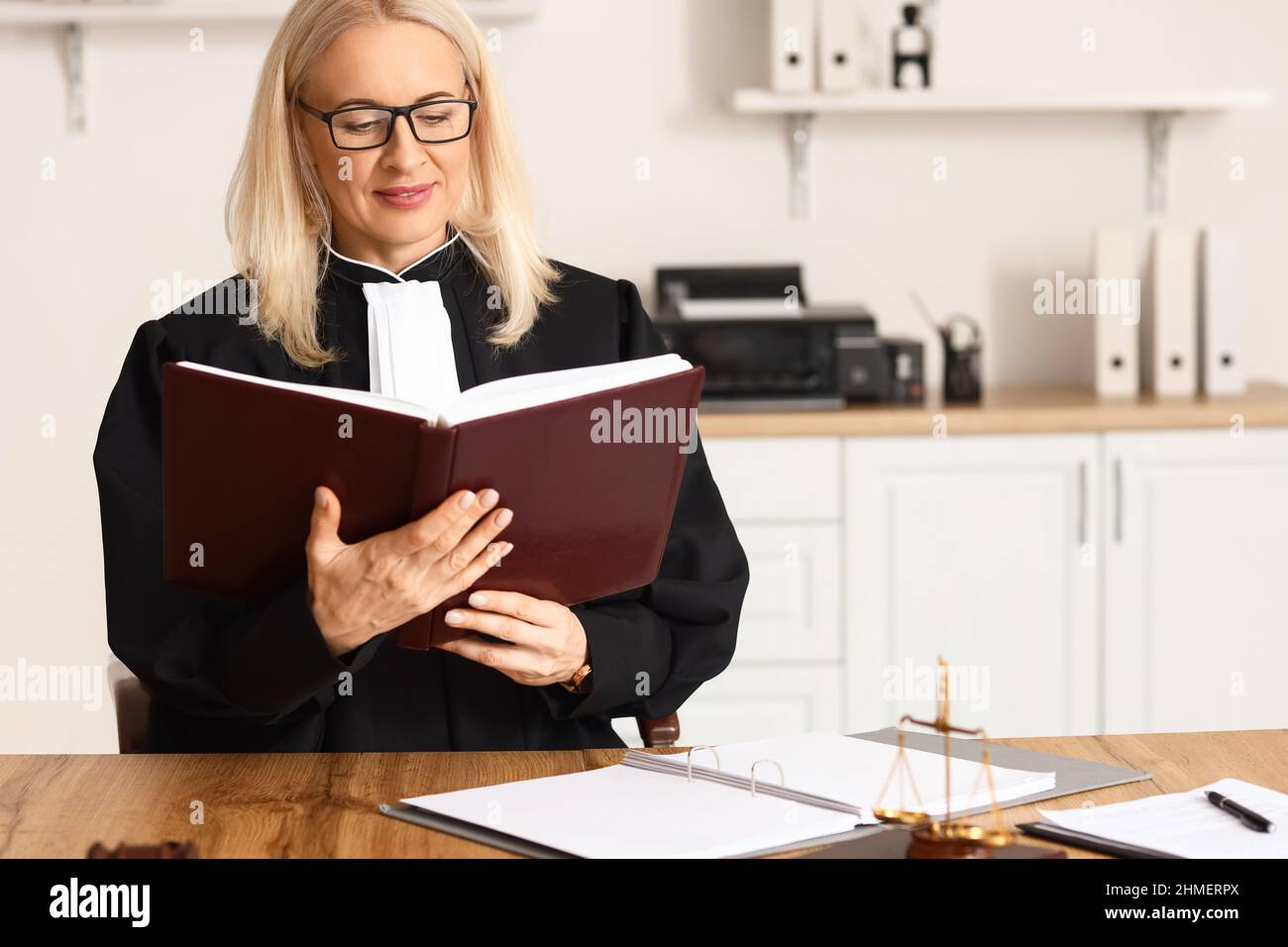 Mature female judge reading book at table in courtroom Stock Photo - Alamy