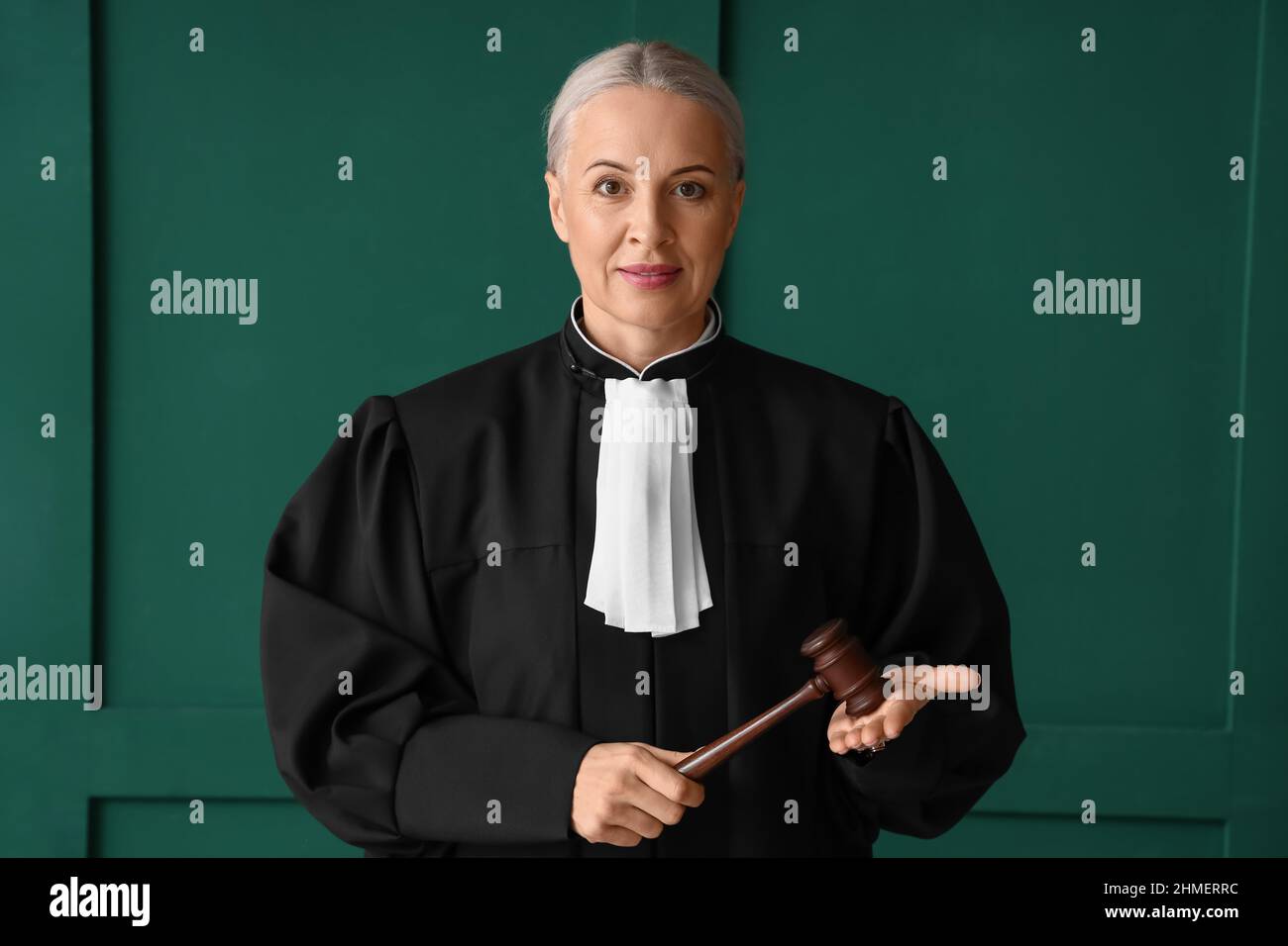 Mature female judge with gavel on green background Stock Photo - Alamy