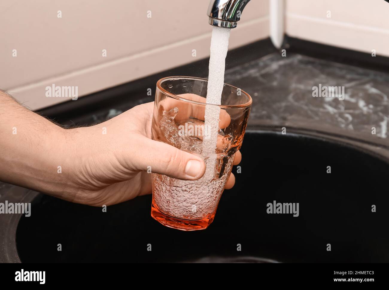 Man filling glass with water from tap in room, closeup Stock Photo - Alamy