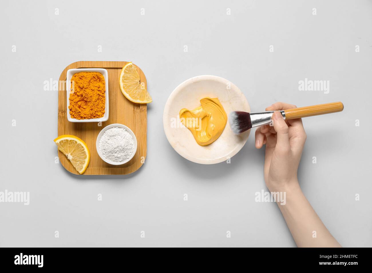 Female hand with brush, bowl with turmeric mask, powder and lemon on ...
