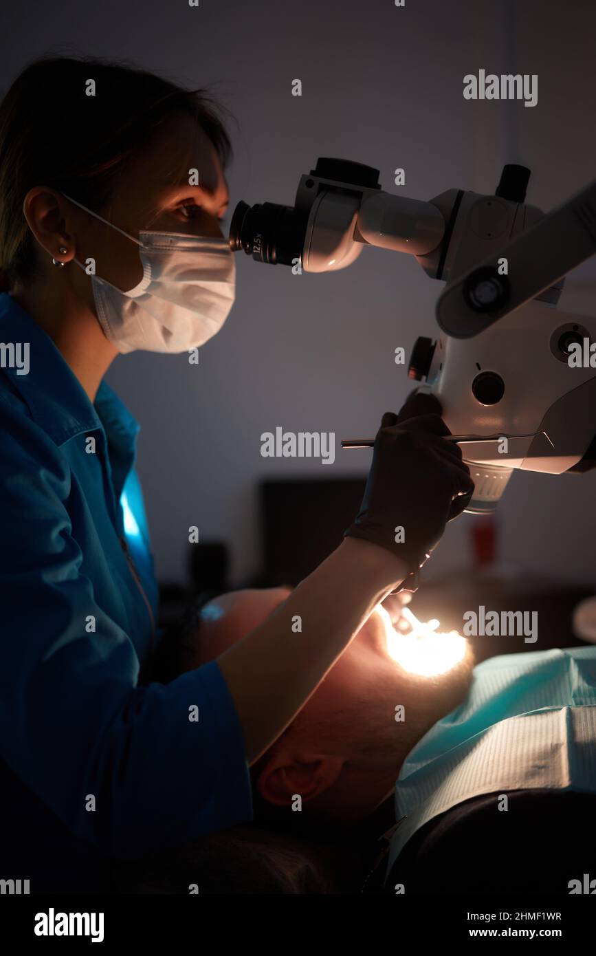 The dentist treats his patient's teeth with a microscope. The dentist ...