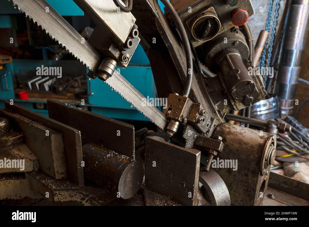 A metal band saw in the workshop cuts a metal rod with a liquid ...