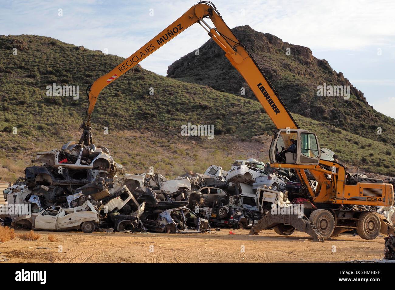 Crane piles scrap car on top of other cars, behind it mountain, scrap ...