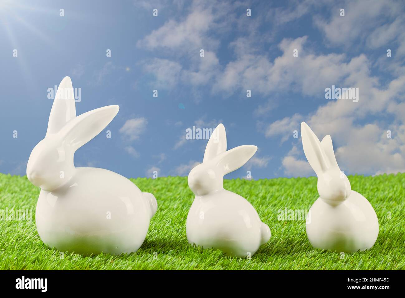 Easter, three porcelain rabbits on a green meadow, blue sky with clouds ...