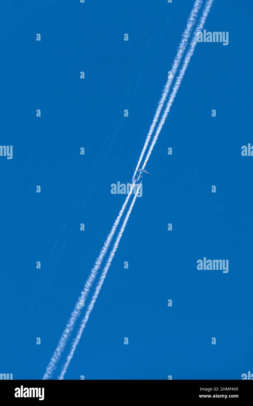 Vertical shot of airliners with a large contrail flying across a clear blue sky Stock Photo - Alamy