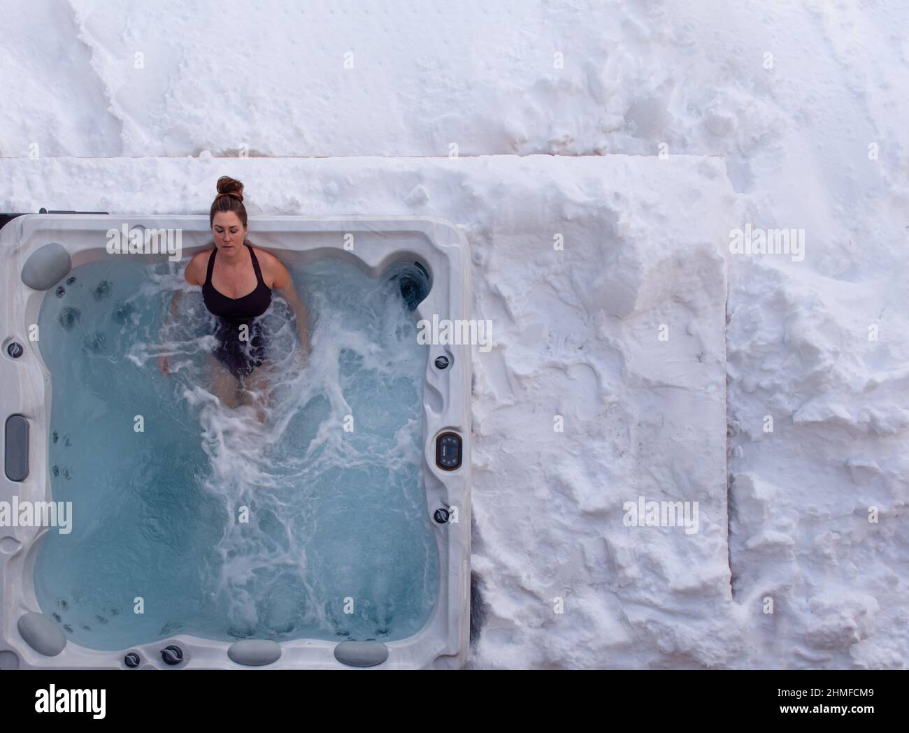 Overhead of woman relaxing in hot tub on snow covered deck in winter ...
