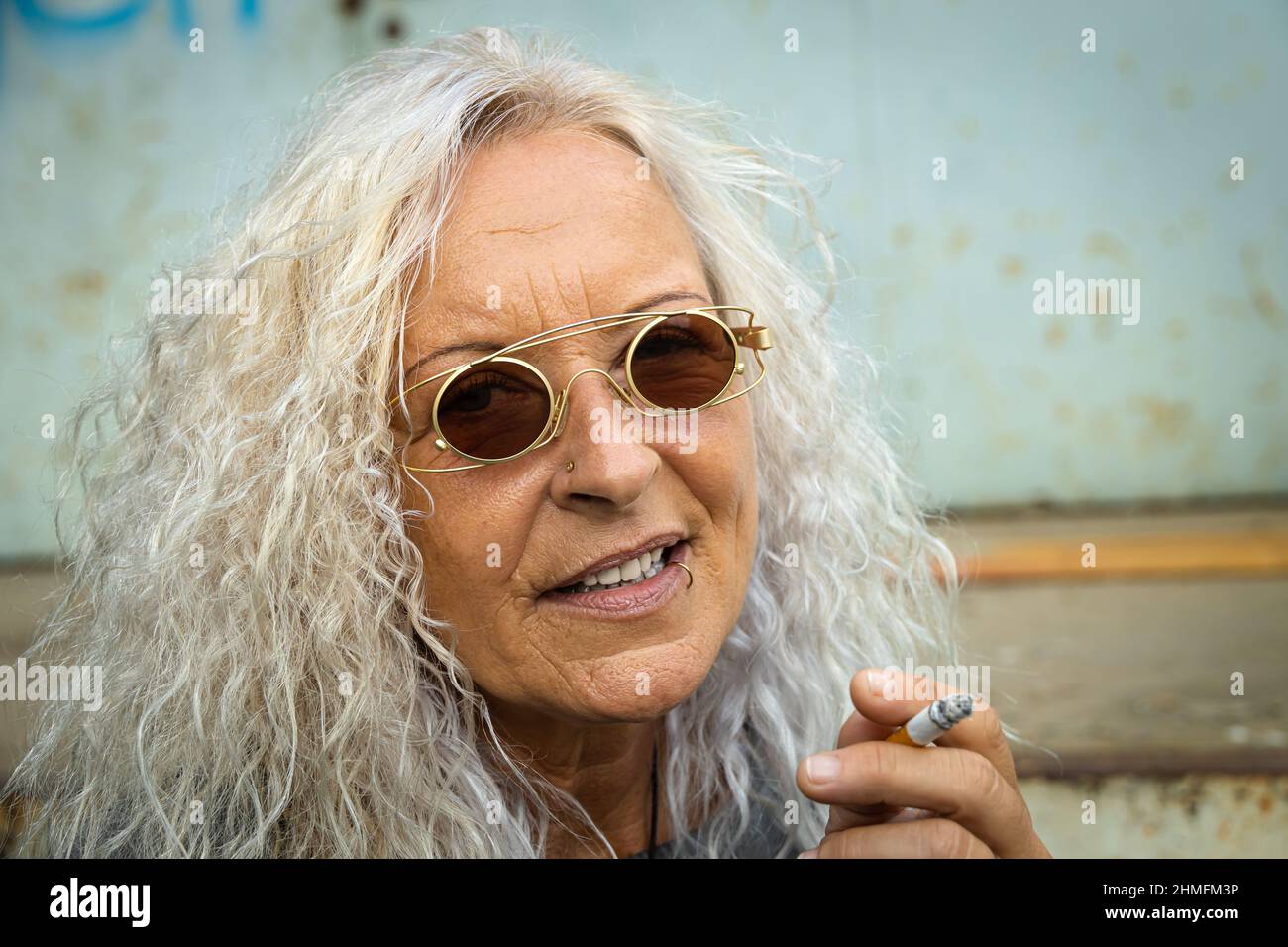 Beautiful woman with long bright curly hair is smoking a cigarette ...