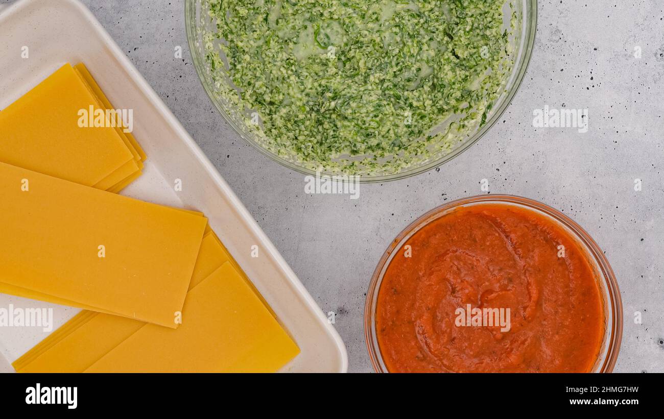 Uncooked lasagna noodles, bowl of marinara sauce, and bowl of spinach ...