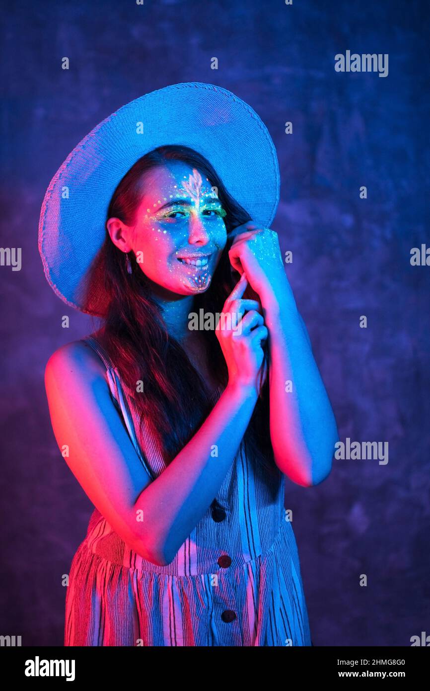 Young woman in hat with fluorescent body art on posing in ultraviolet ...
