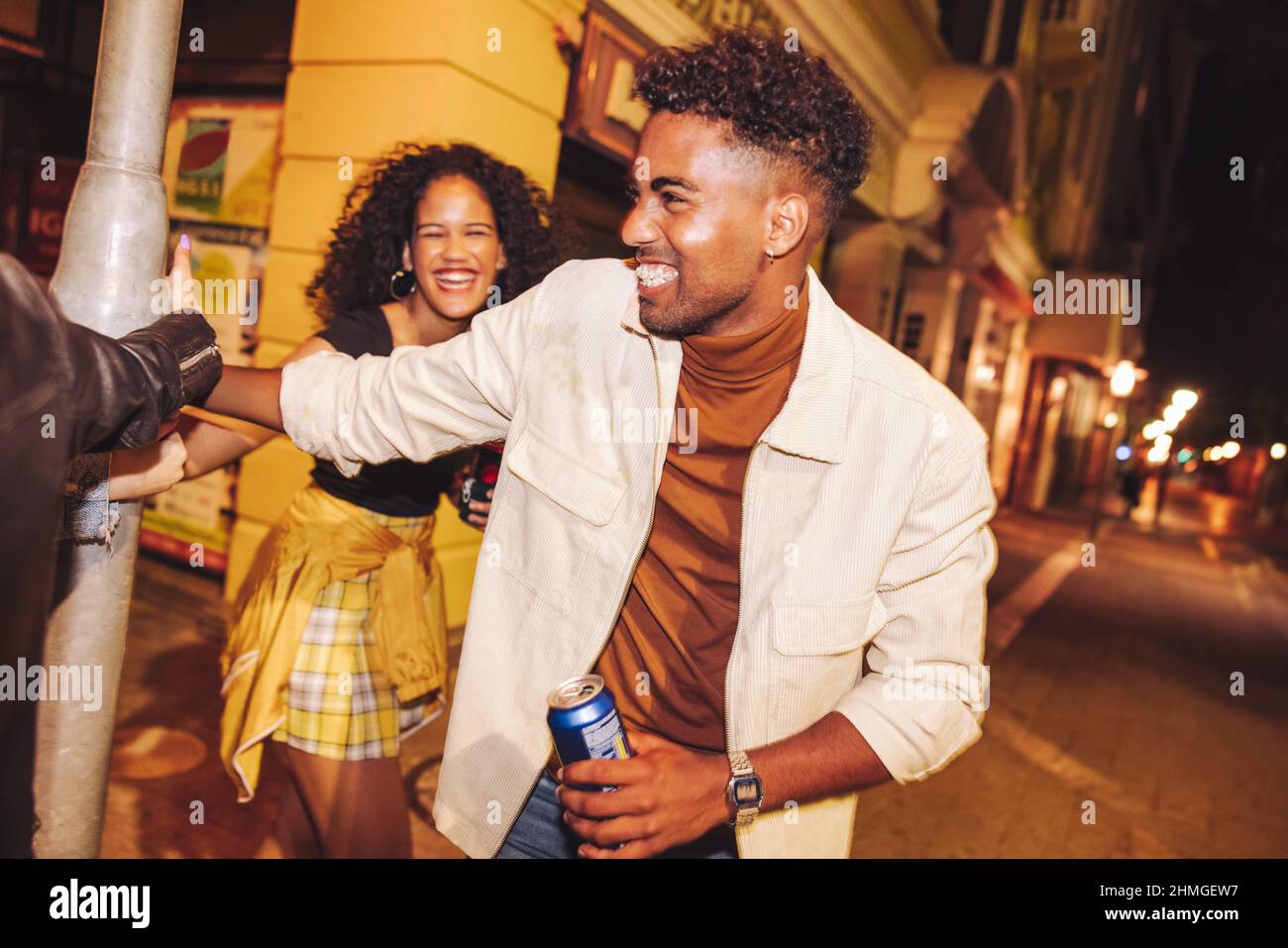 Joyful friends playing around a pole at night. Group of cheerful young ...