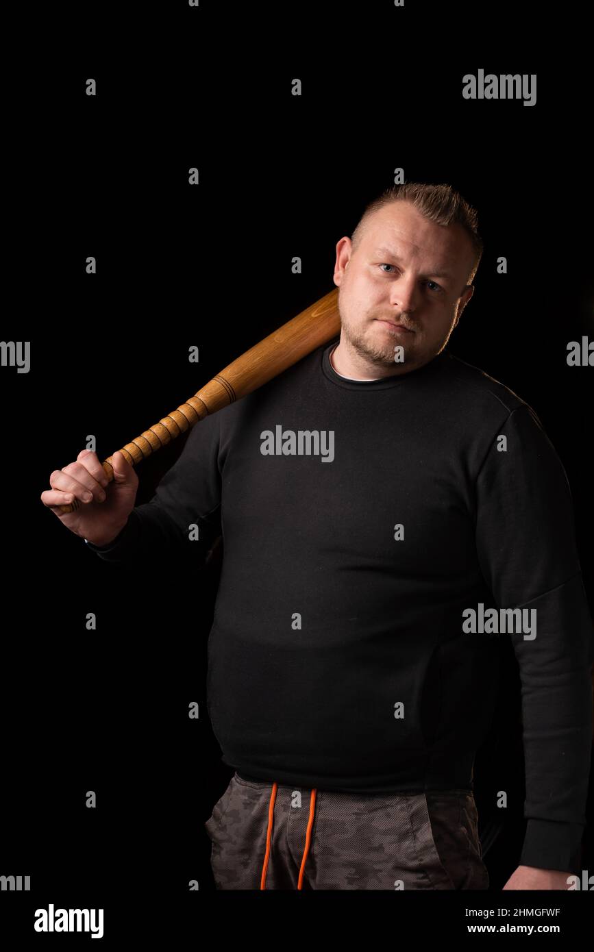 A young strong man holds a bat in his hand. Dark background. A large ...