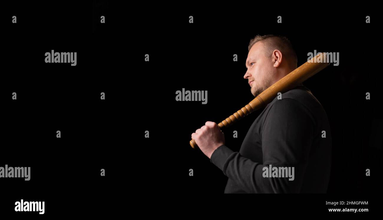 Young man with a baseball bat on a dark background. Bouncer, security ...