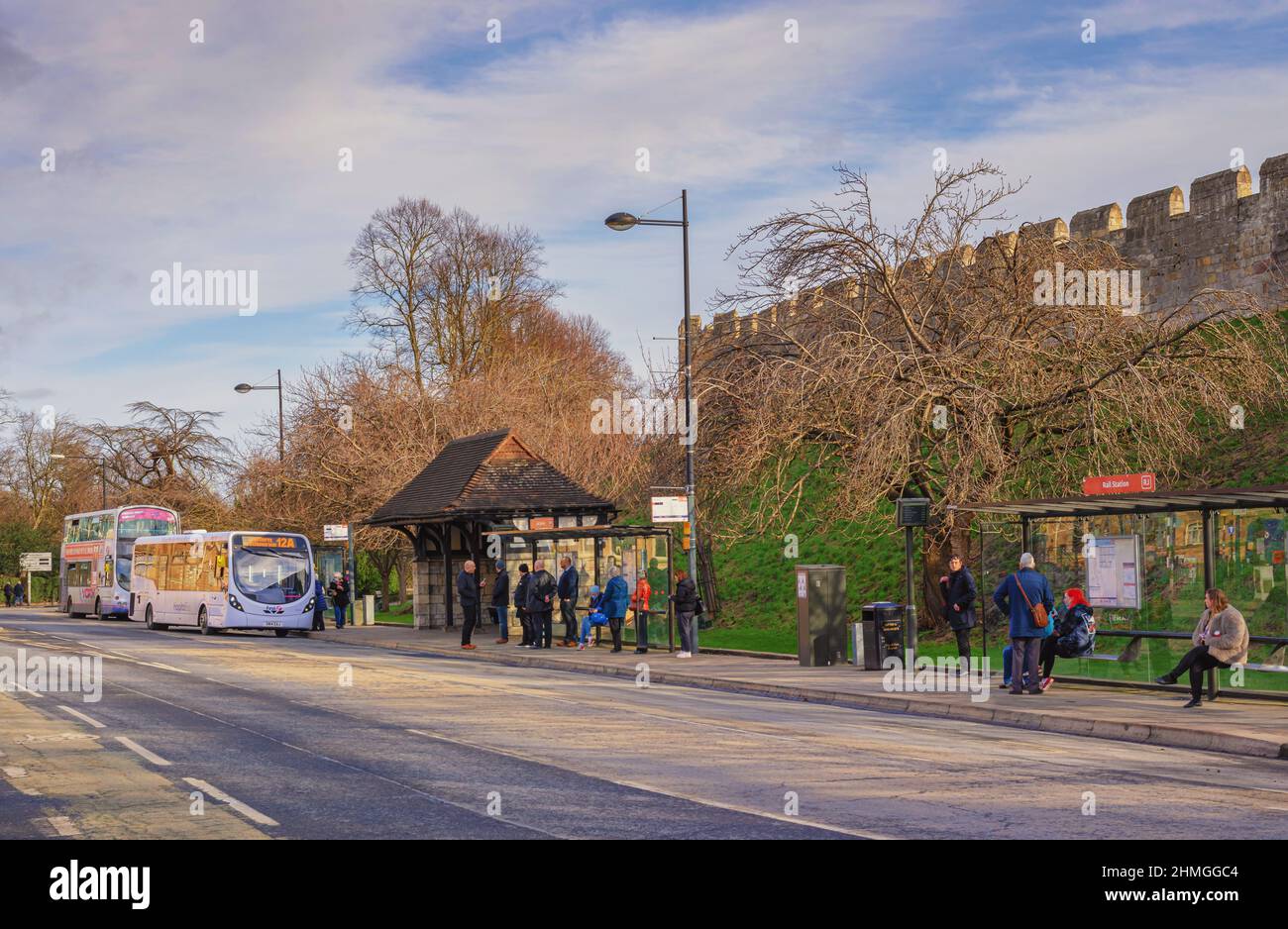 A bus stop and buses underneath historic city walls. Passengers wait ...