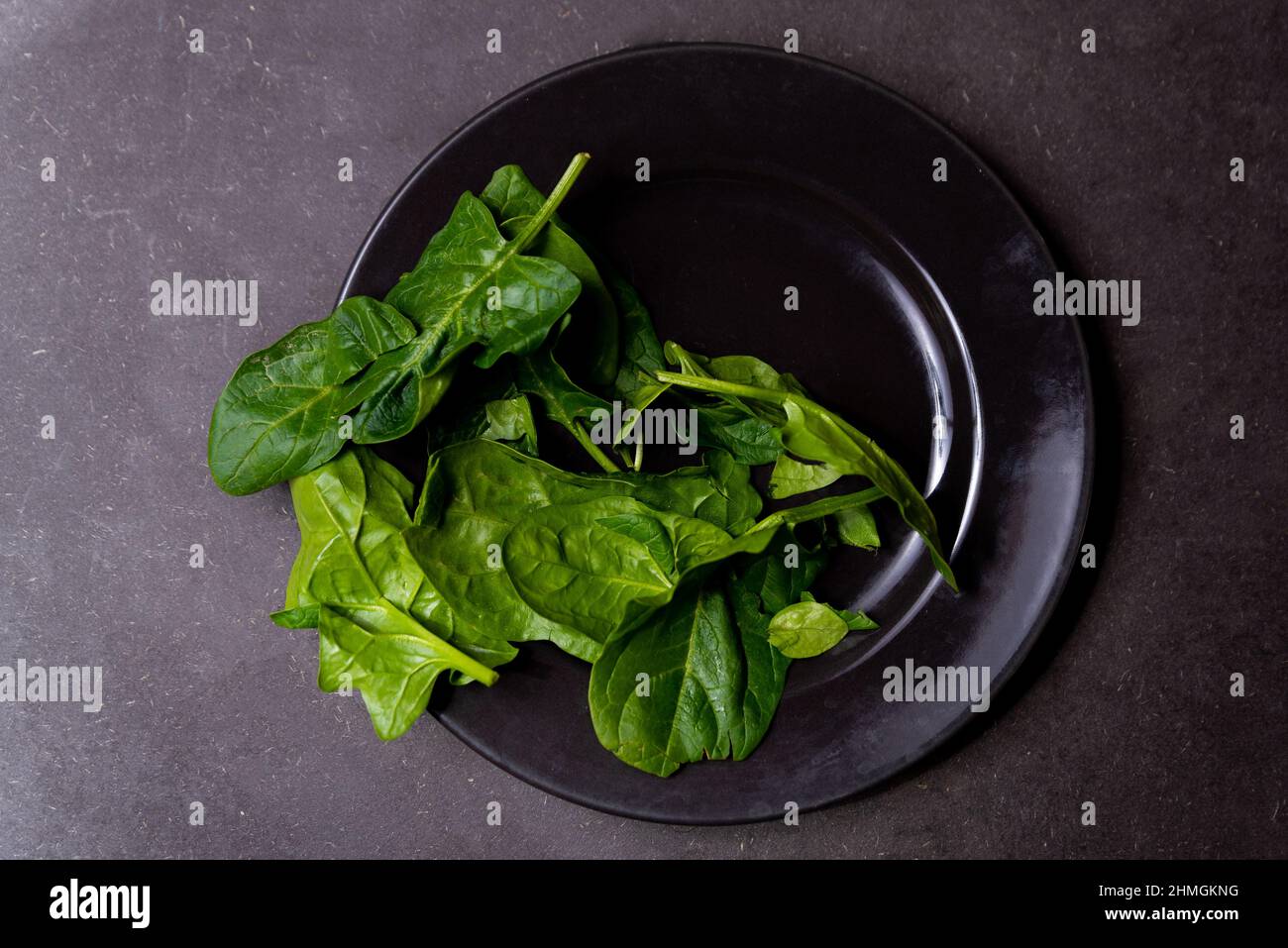 fresh green spinach leaves on dark black table in black dish top view ...