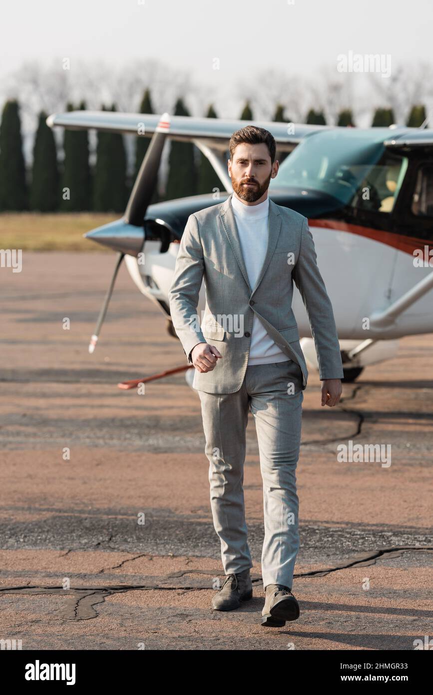 full length of bearded businessman in formal wear walking near ...