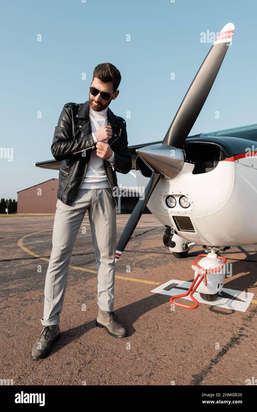 full length of stylish pilot in leather jacket and sunglasses smiling ...