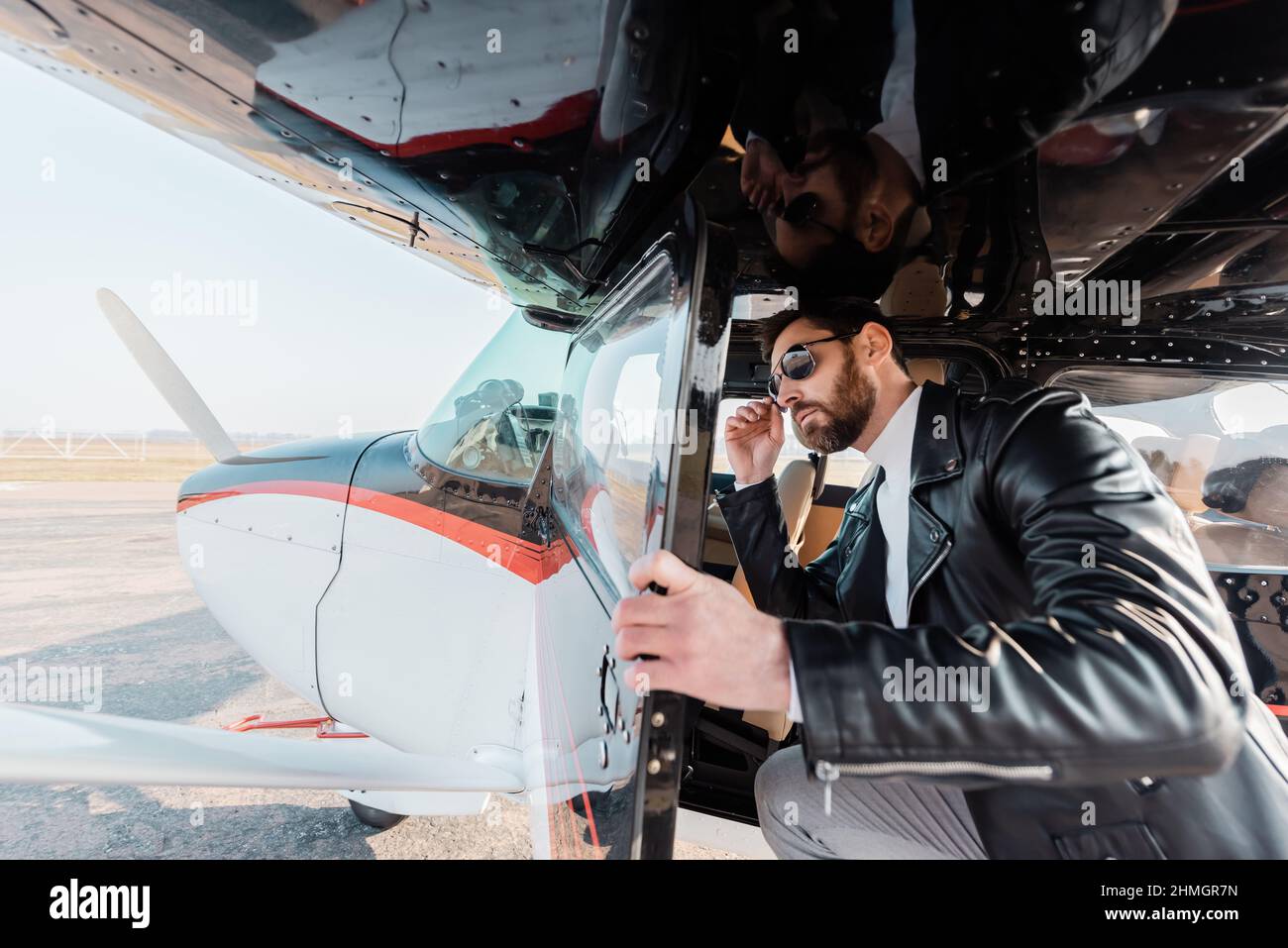 bearded pilot adjusting stylish sunglasses and opening door in ...