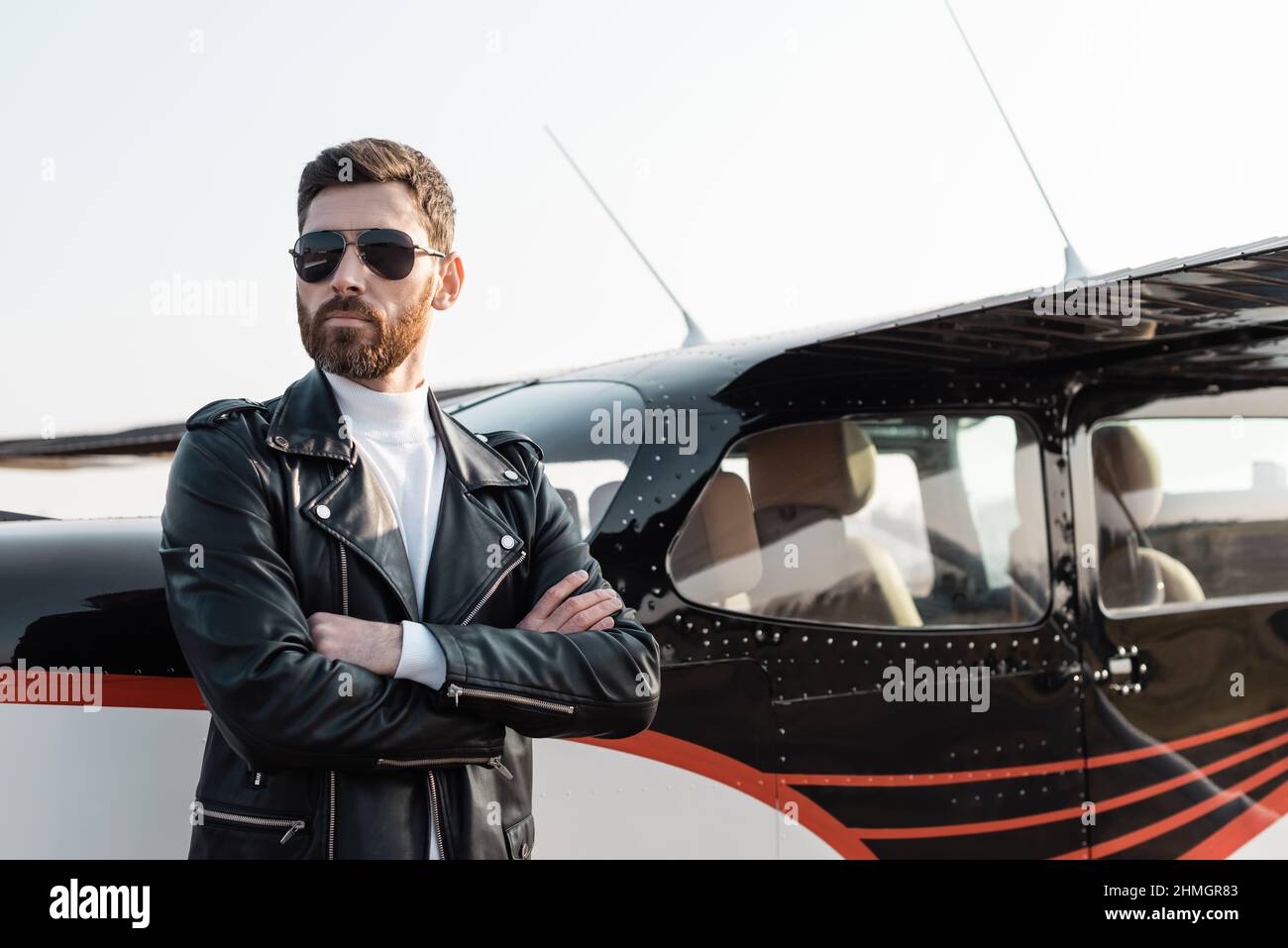bearded pilot in sunglasses and leather jacket standing with crossed ...
