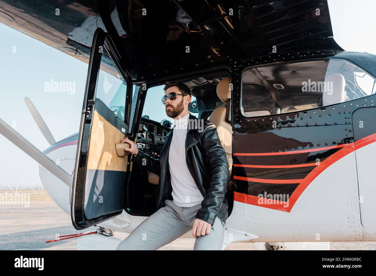bearded pilot in stylish sunglasses and leather jacket leaning on ...