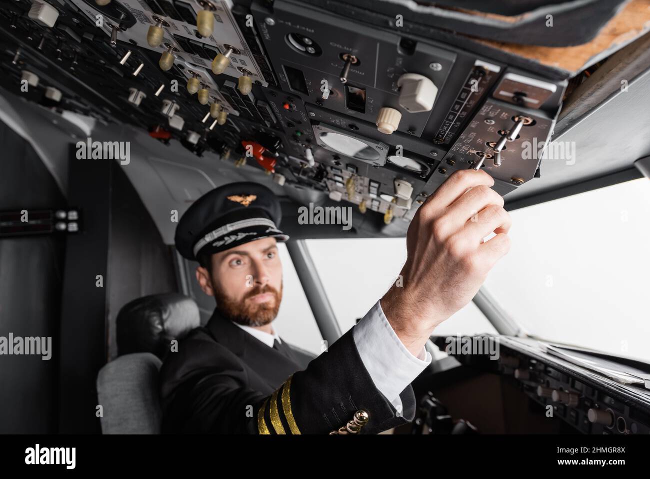 pilot in cap and uniform reaching overhead panel in airplane simulator ...