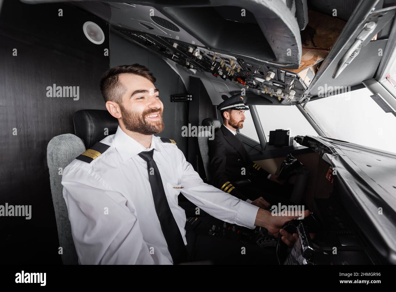 smiling co-pilot using yoke near captain while piloting in airplane ...