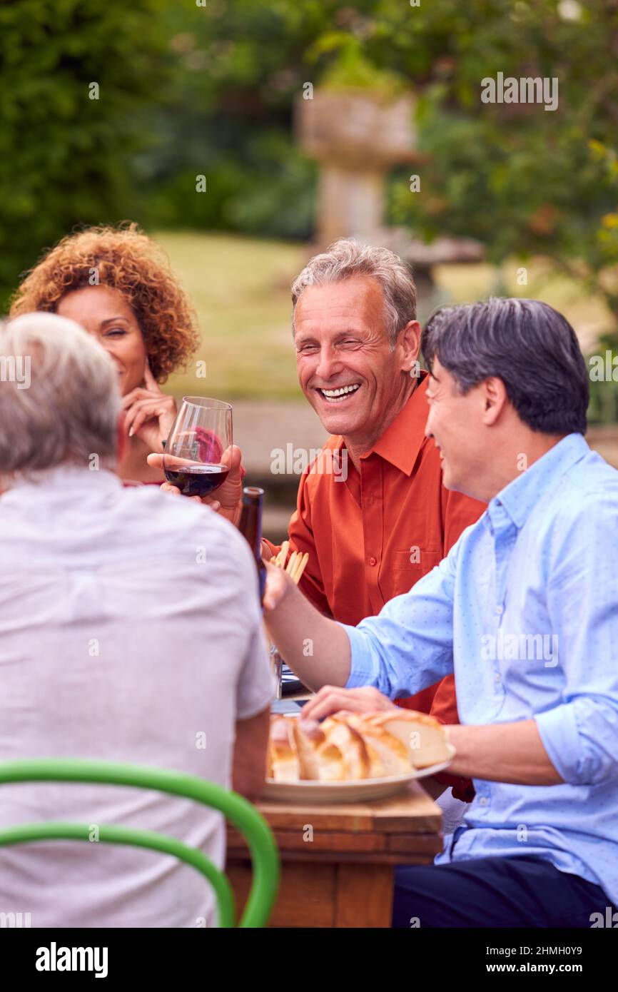 Group Of Mature Friends Talking Around Table At Summer Dinner Party In ...