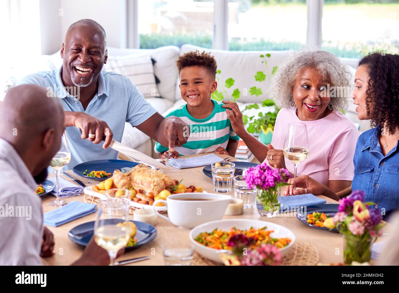 Grandfather Carving As Multi Generation Family Sit Around Table At Home ...