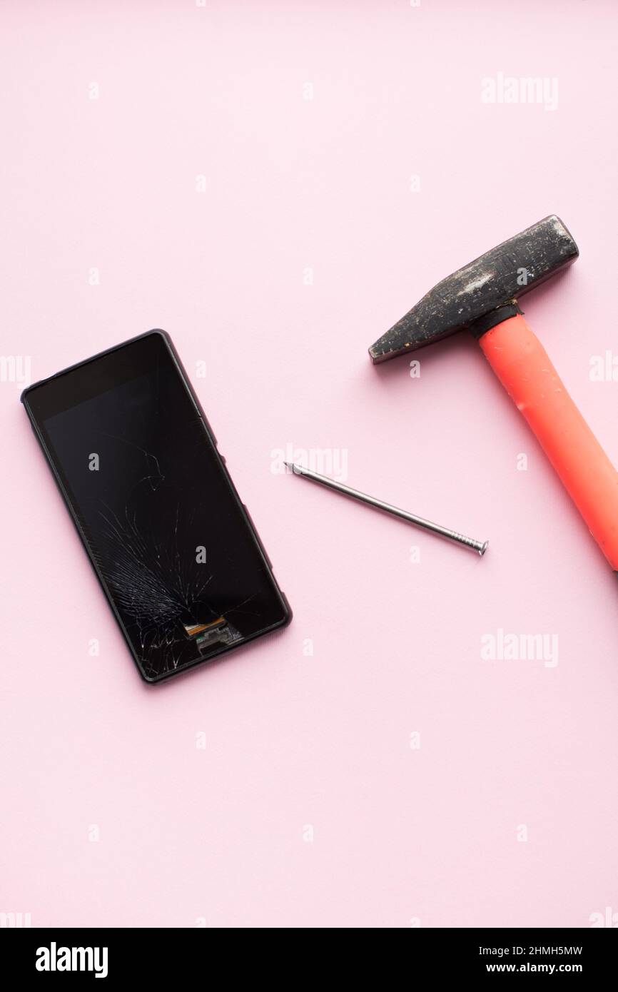 Hammer, nail and mobile phone with broken display on pink background ...